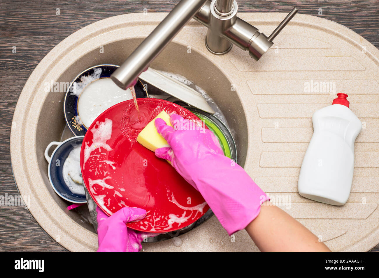 Close up hands of woman washing dishes in kitchen. Hands in red rubber ...