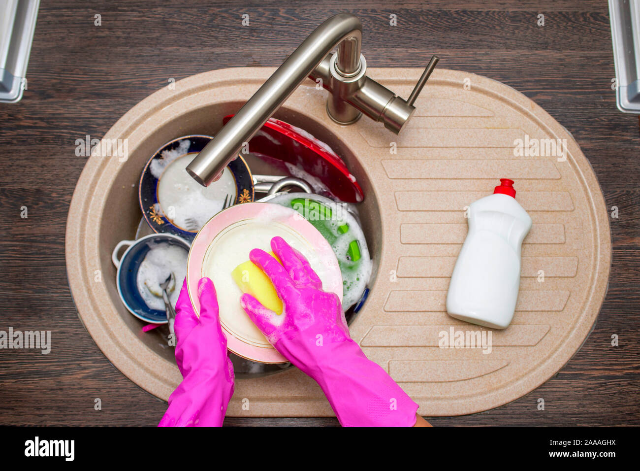 Close up hands of woman washing dishes in kitchen. Hands in red rubber ...