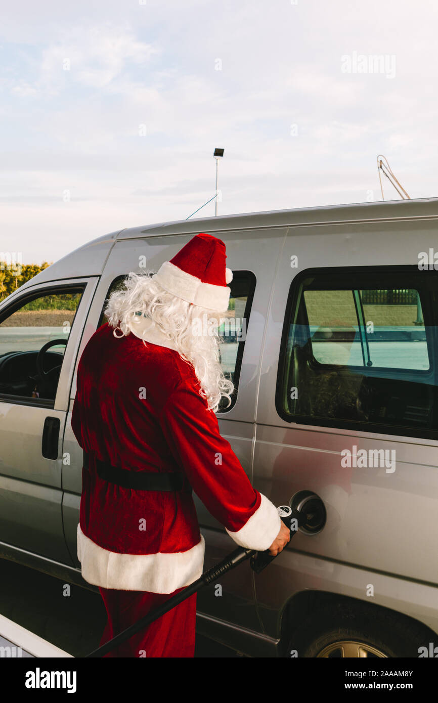 Santa Claus working as a delivery man and fueling up in his van car in ...