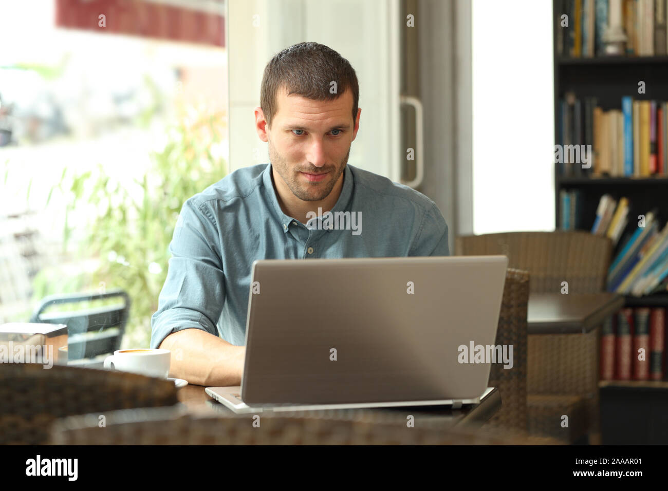 Serious man typing on laptop entering data sitting in a coffee shop ...
