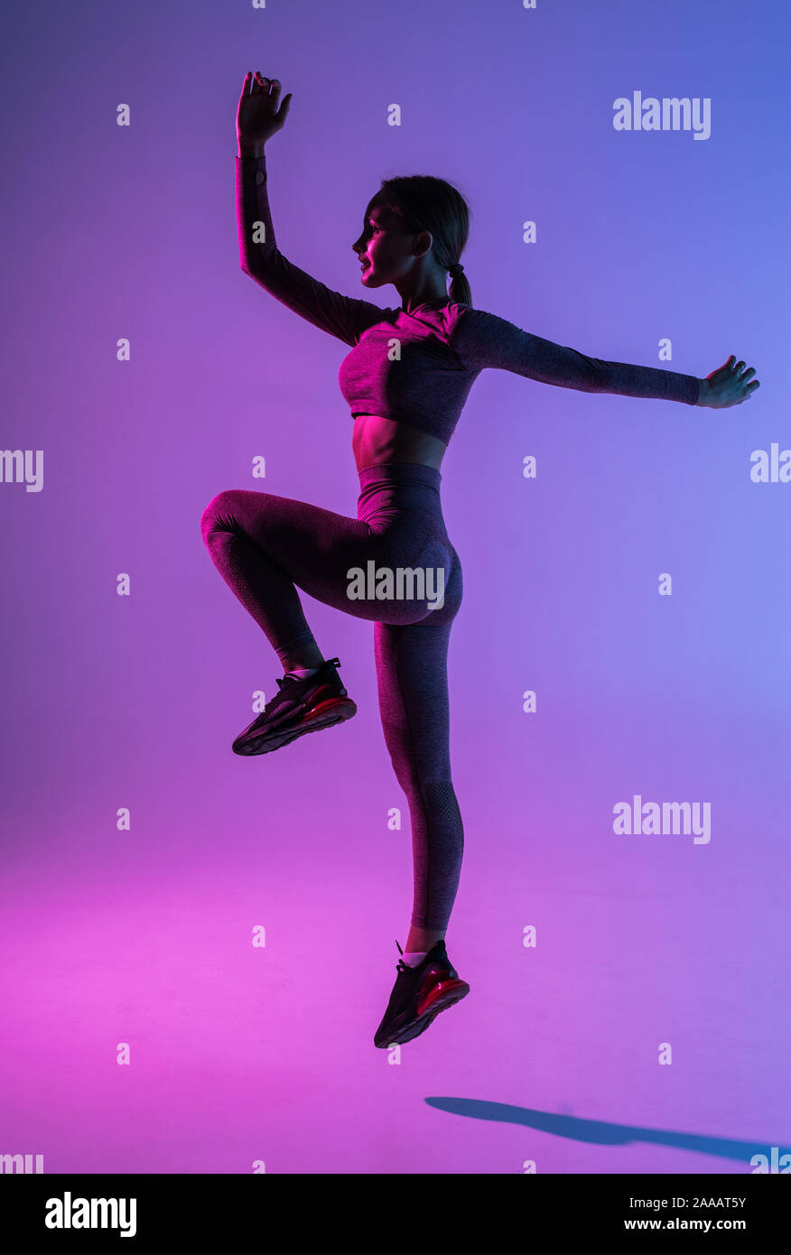 Side view of a sporty young woman jumping isolated on purple light ...