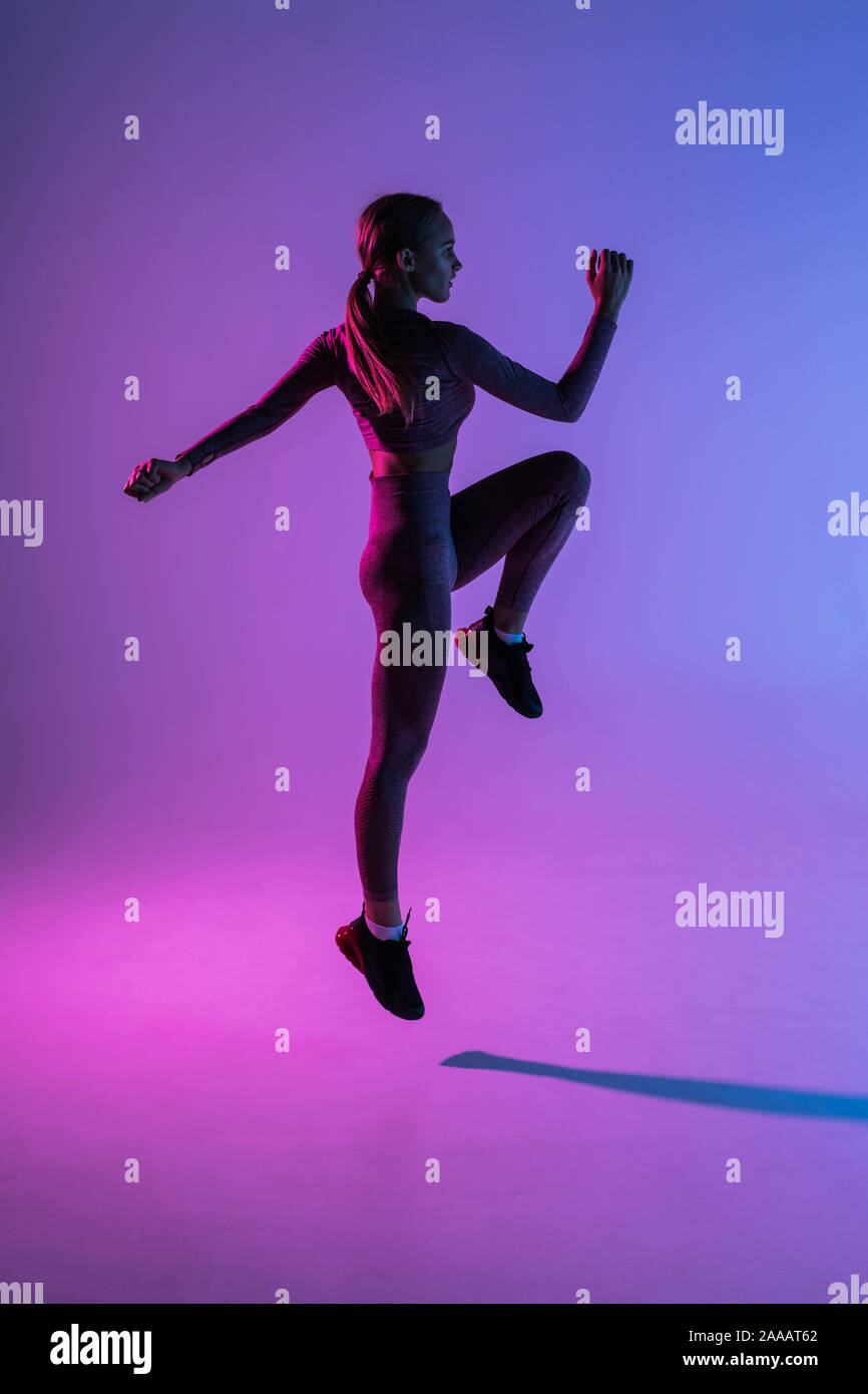 Side view of a sporty young woman jumping isolated on purple light ...