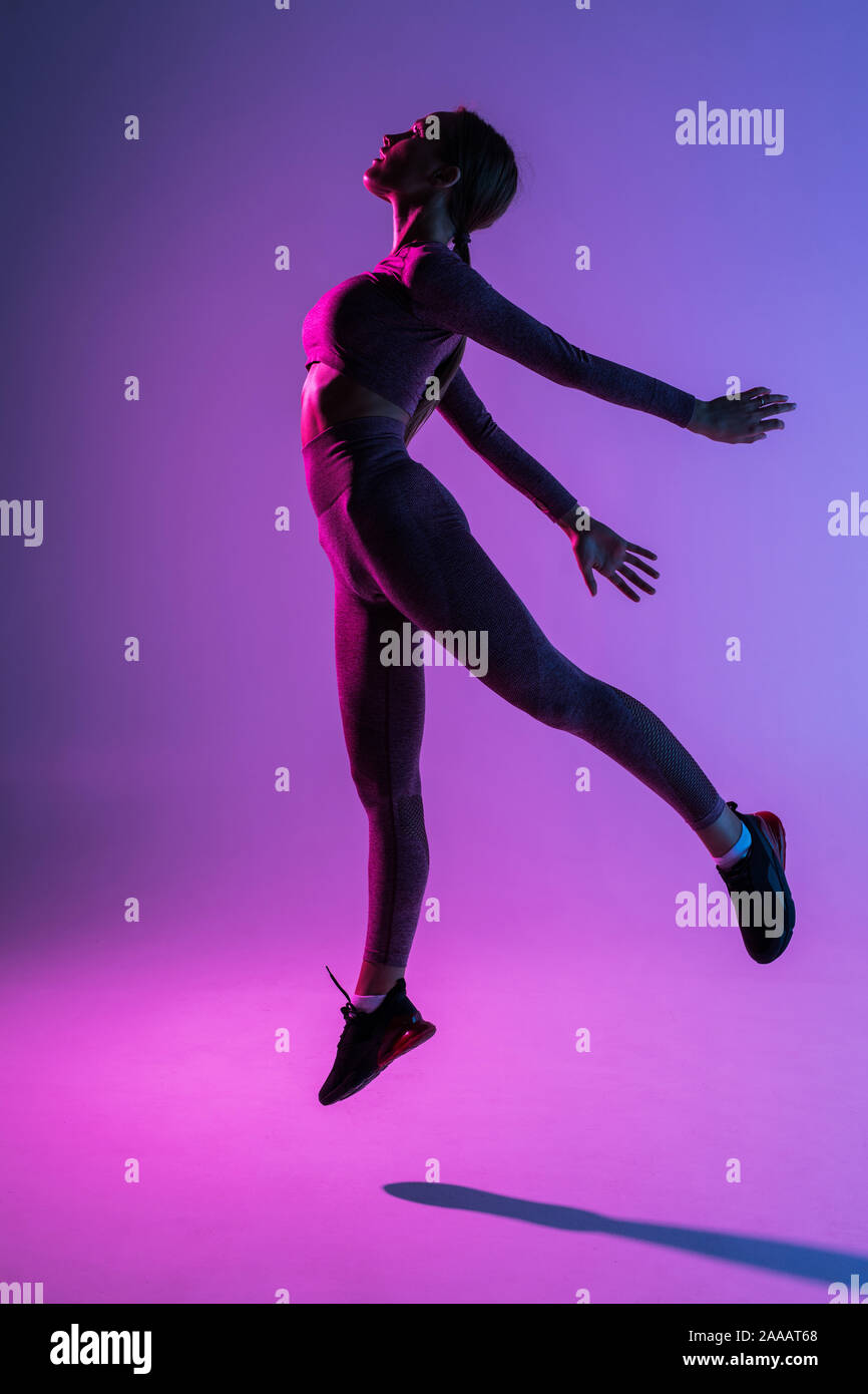Side view of a sporty young woman jumping isolated on purple light ...