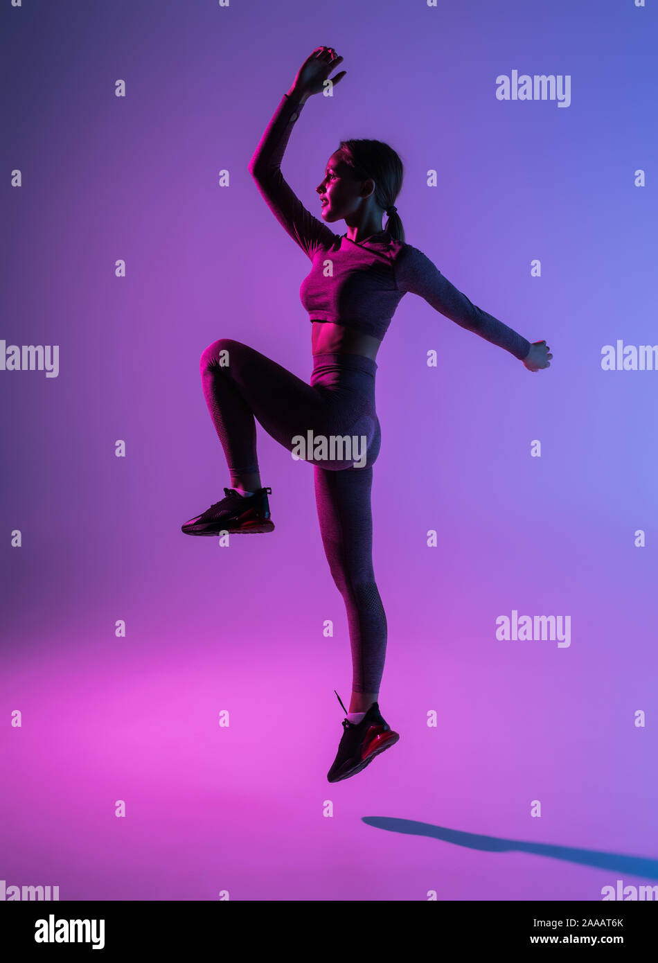 Side view of a sporty young woman jumping isolated on purple light ...