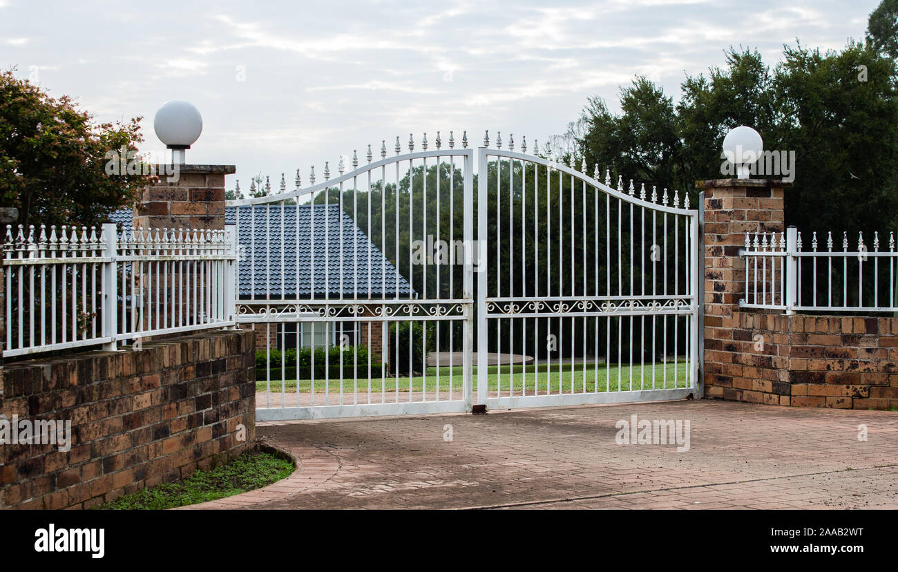 White metal wrought iron driveway property entrance gates set in brick ...