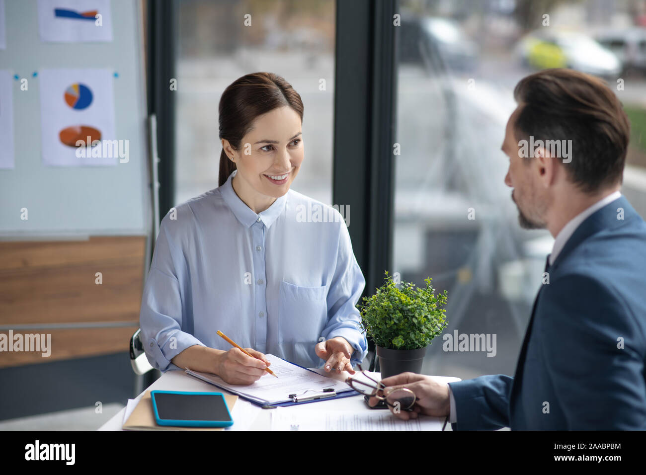 Smiling assistant talking to businessman and making some notes in the ...