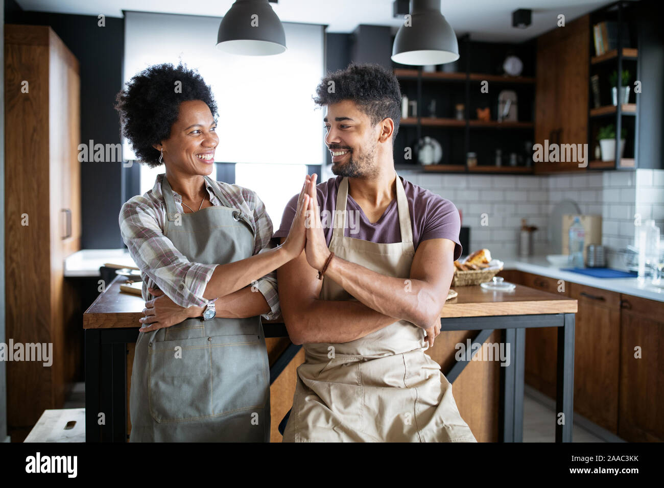 Young happy couple in aprons giving high five in kitchen Stock Photo ...