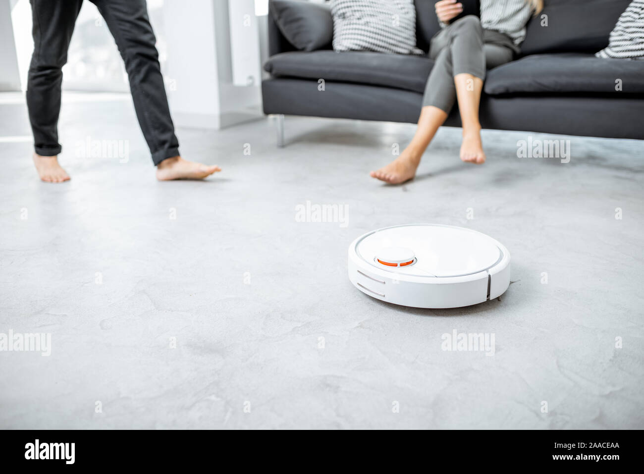 Automatic vacuum cleaner working on the floor, couples legs on the ...