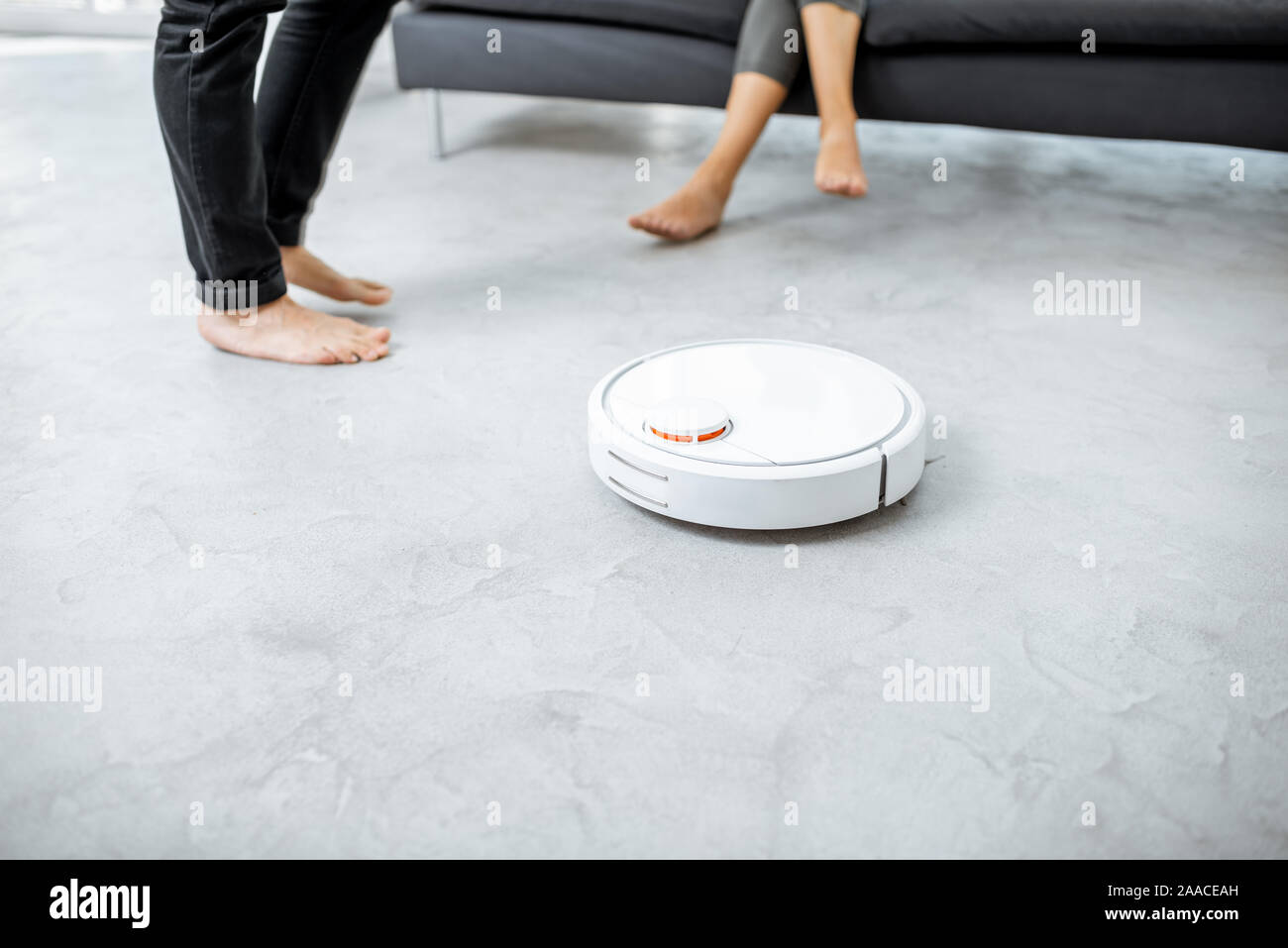 Automatic vacuum cleaner working on the floor, couples legs on the ...