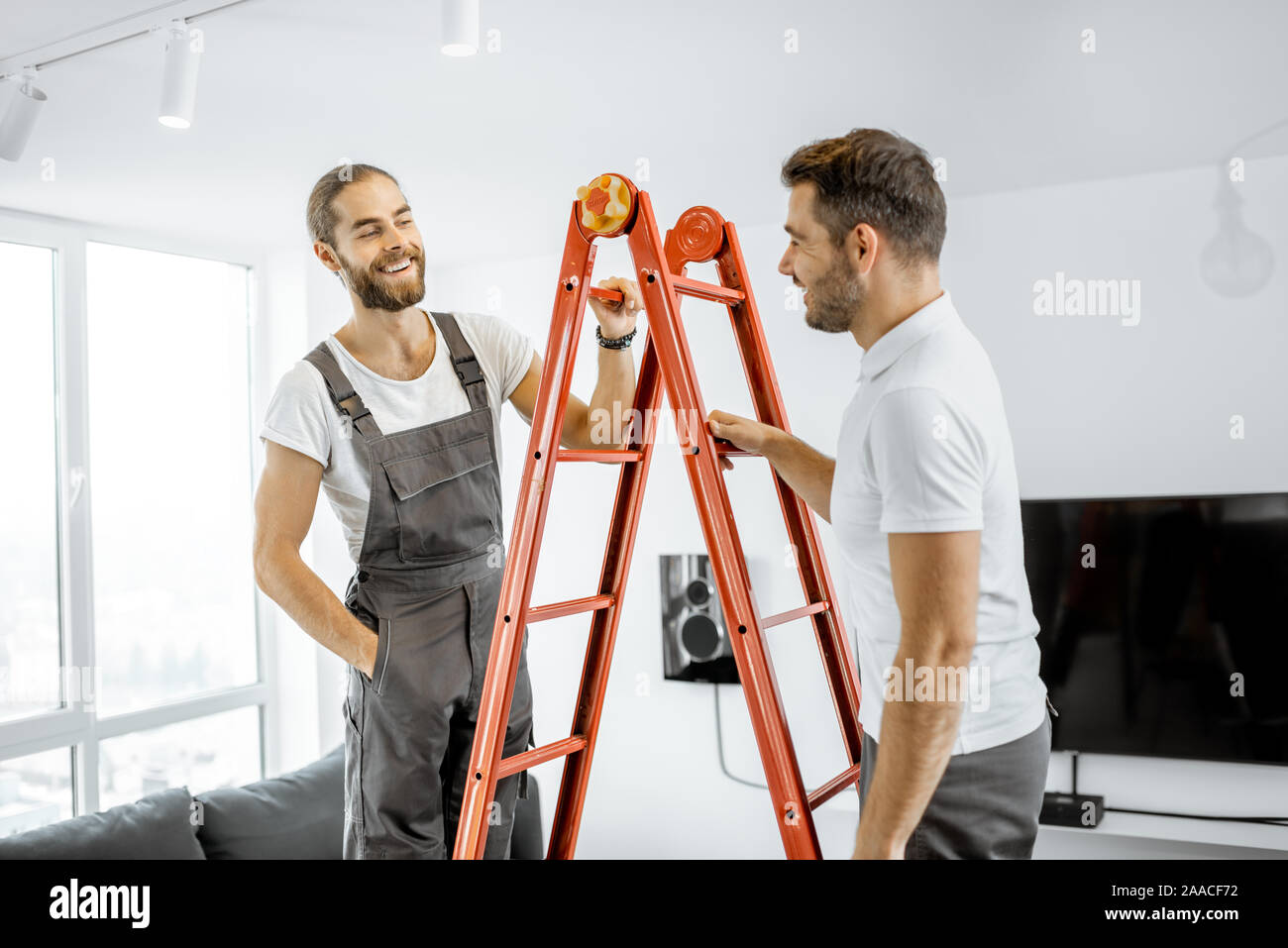 Two handsome workmen in uniform talking on the ladder during some ...