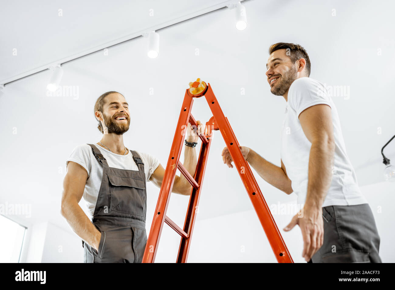 Two handsome workmen in uniform talking on the ladder during some ...