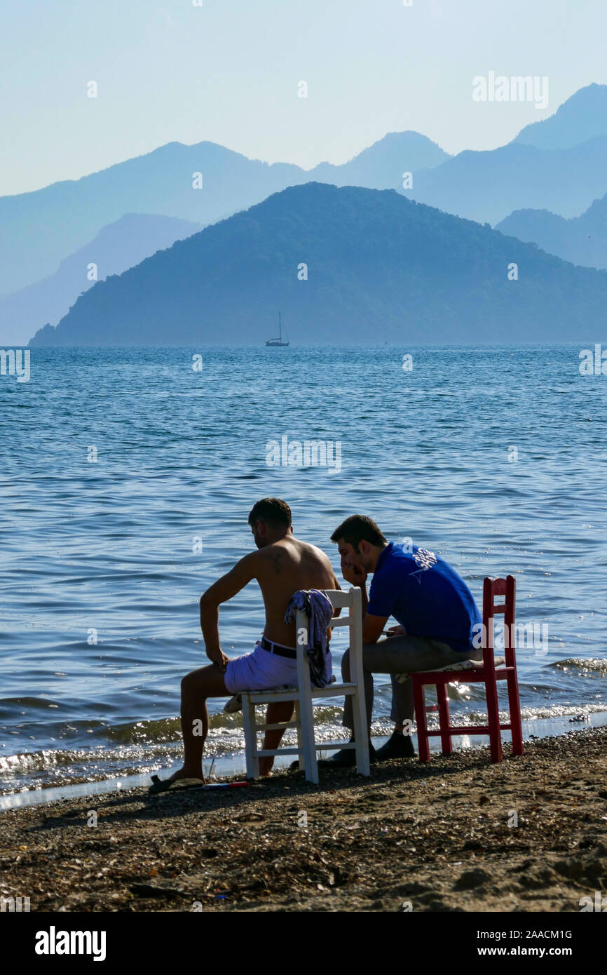 Two men sat on chairs on beach in Marmaris holiday resort, Mugla ...