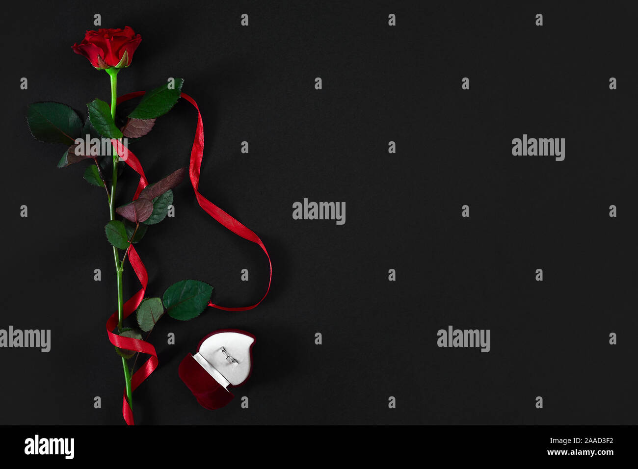 One dark red rose with red ribbon and box with ring on black bac Stock ...