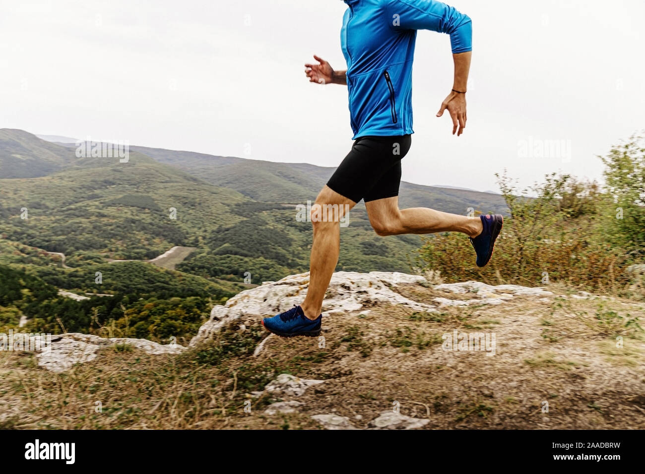 athletic man running mountain trail in blue jacket in background of ...