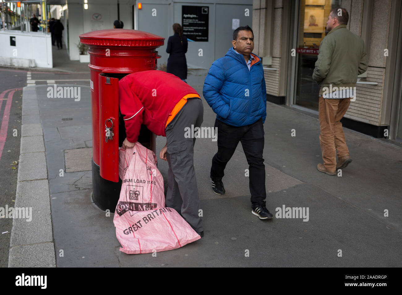 A Royal Mail postal worker leans into a post box to empty a batch of ...