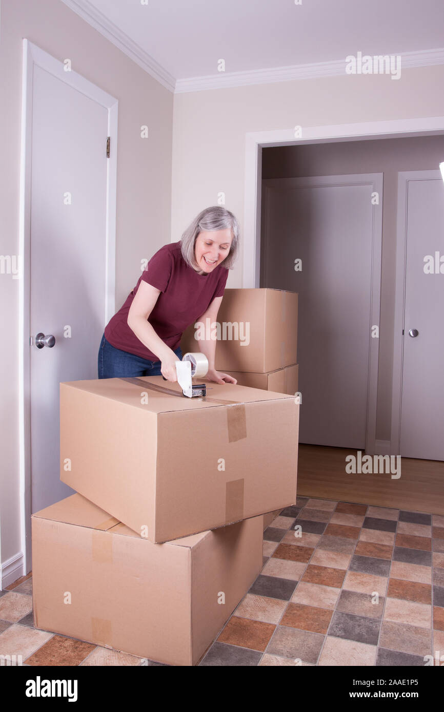 Woman in her early fifties closing a cardboard box with tape for moving ...