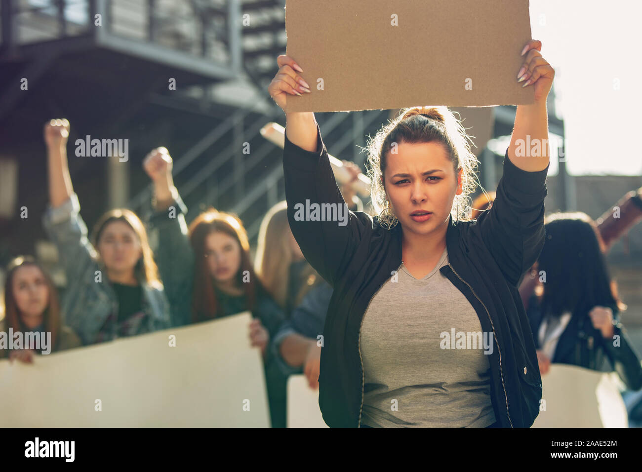 Young woman with blank poster in front of people protesting about women ...