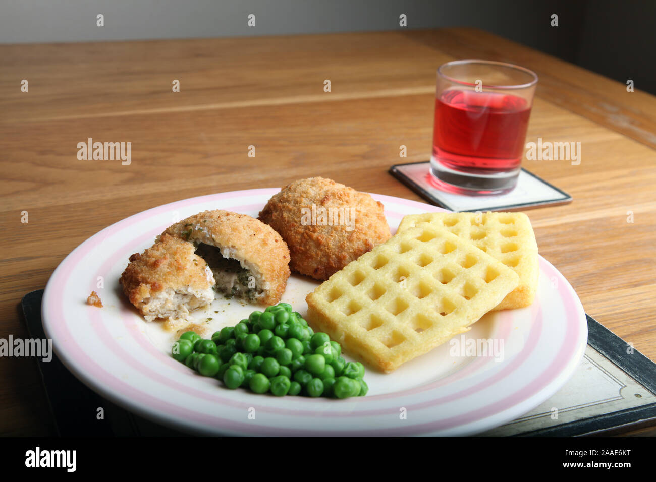 Chicken Kievs cut open with Potato Waffles and Peas on plate served at ...