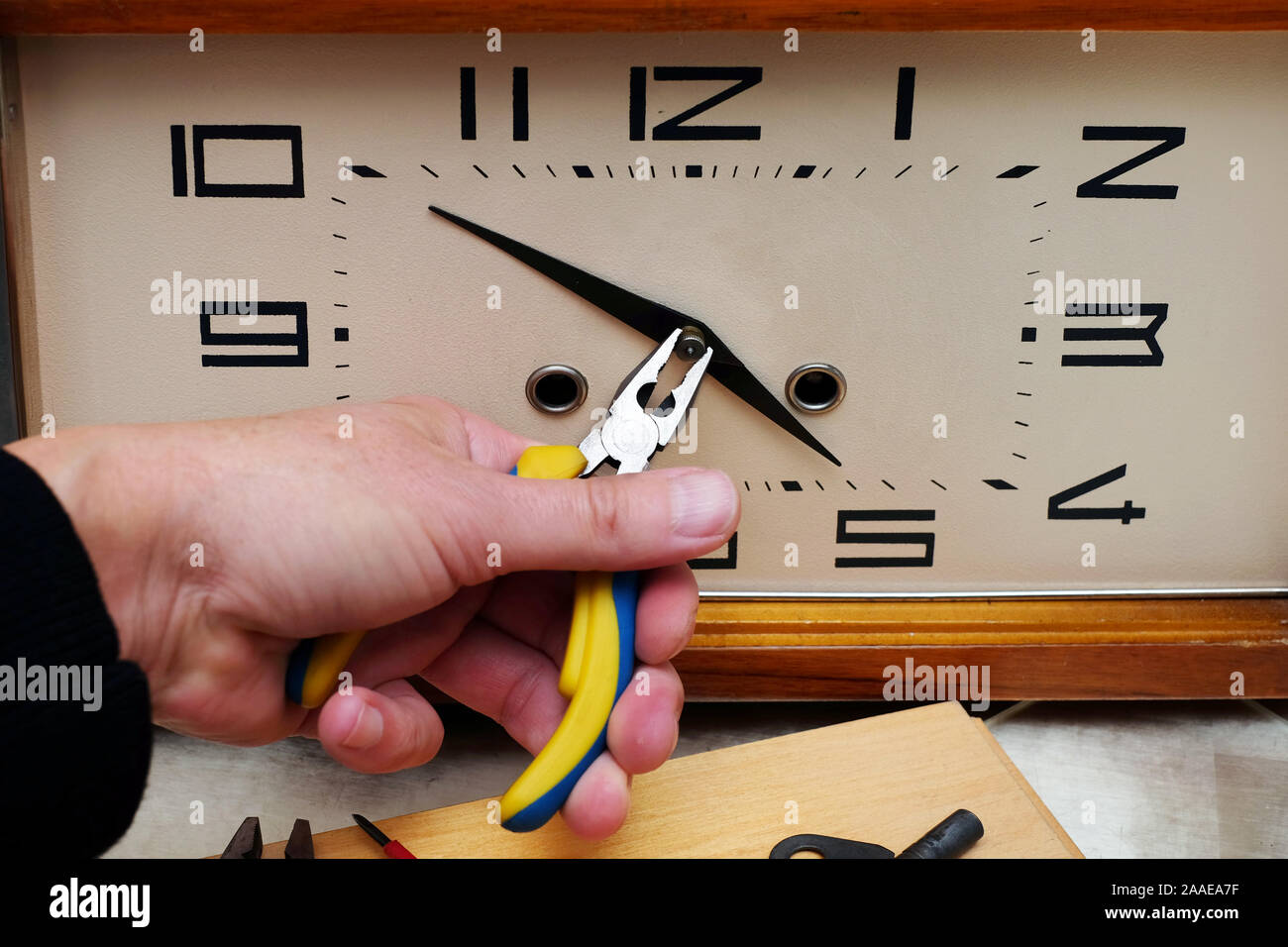 A hand with pliers about to remove clock hands, indoor close-up Stock ...