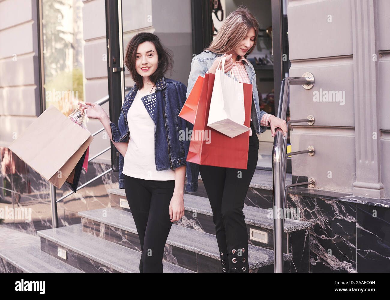 Two young woman carrying shopping bags while walking on the stairs ...