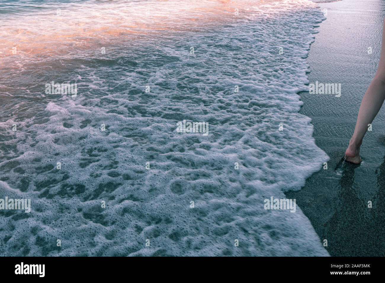 Waves at the beach and female leg going away from the water, not to get ...