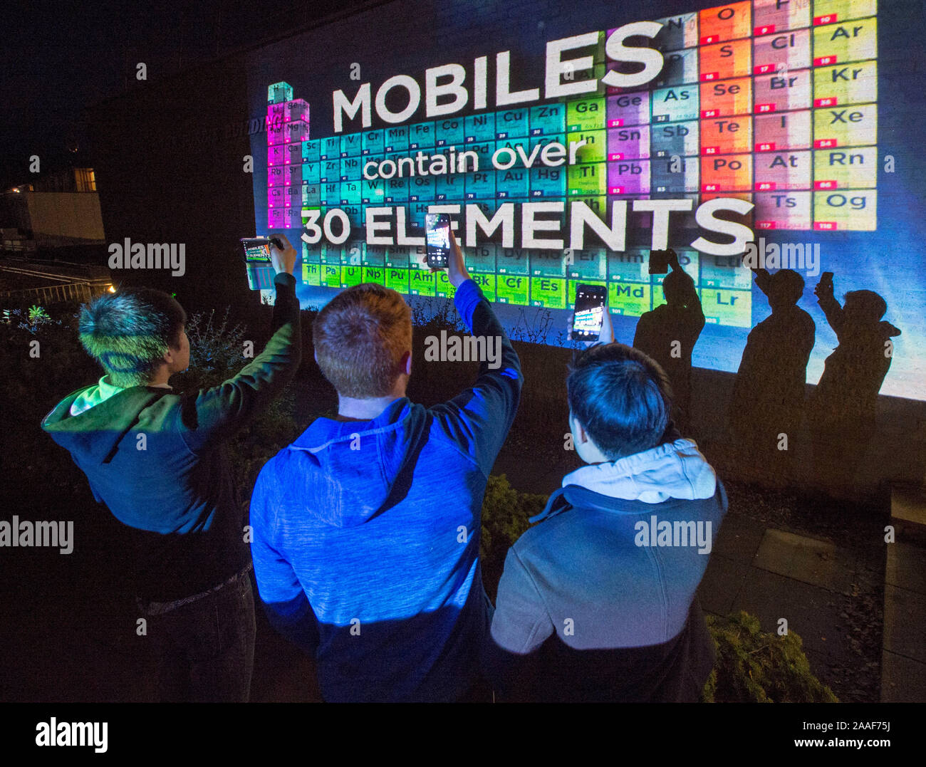 Students hold up mobile phones against a light display at the ...