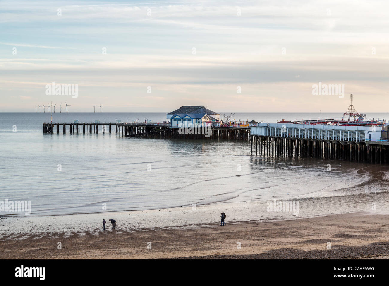 Clacton Pier reaching out into the sea. In the foreground people walk ...