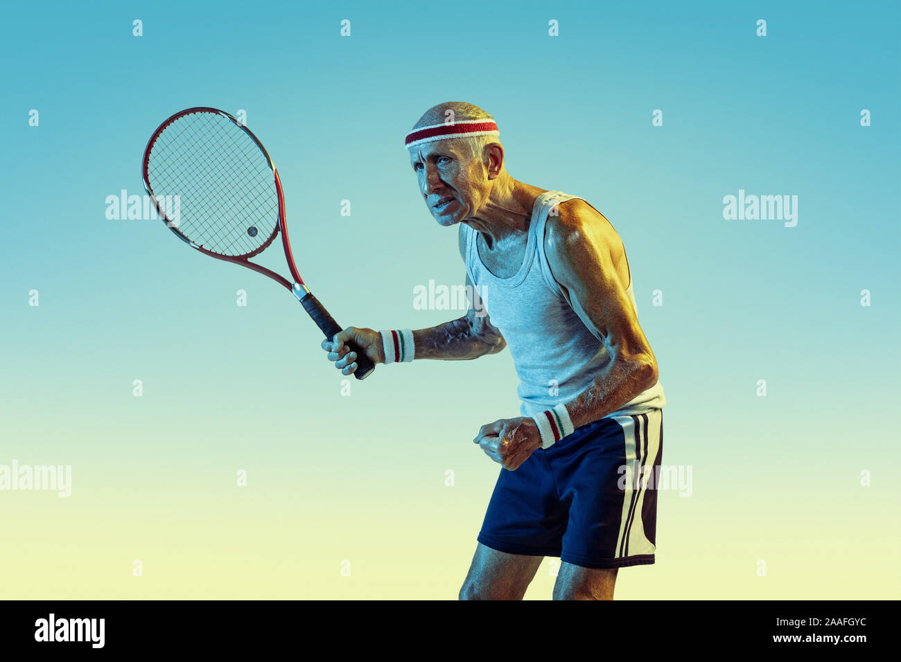 Senior man wearing sportwear playing tennis on gradient background ...