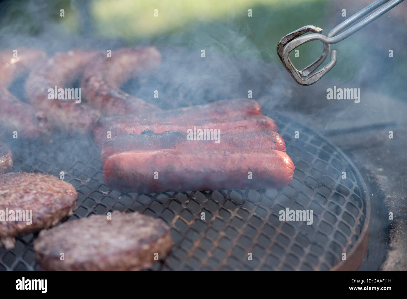 Steel tongs reaching for a hot dog wiener being cooked over an open ...