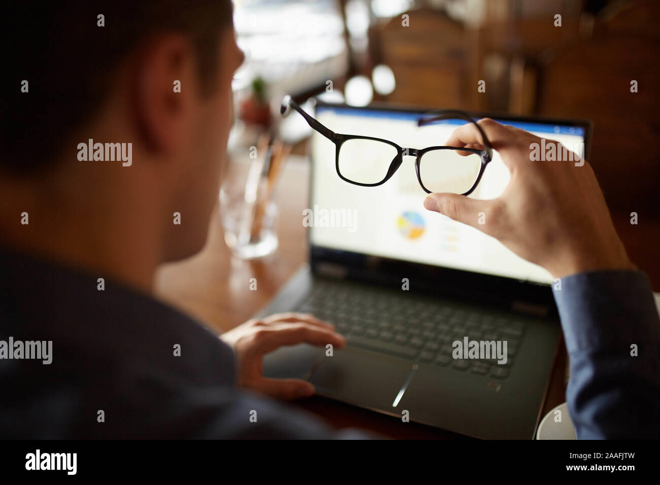 Back view of man hand holding eyeglasses in front of laptop screen with ...