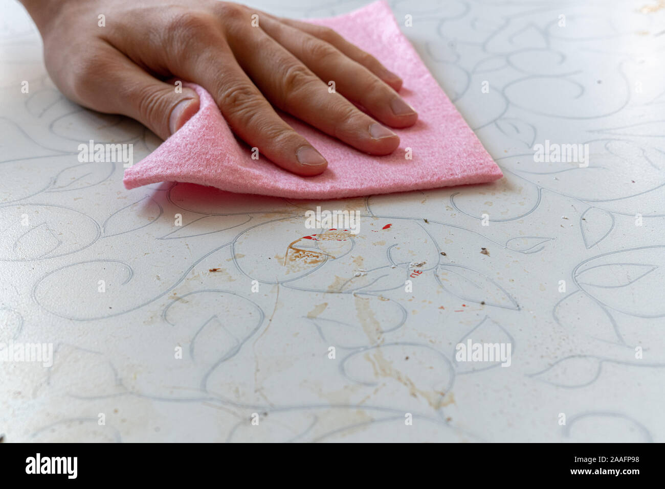 hand with a red rag wiping the dirty table surface in kitchen at home ...