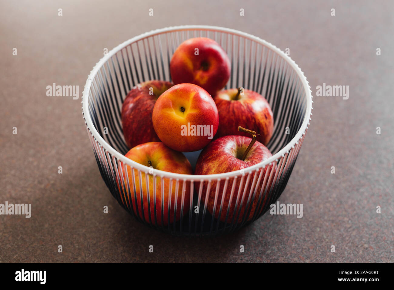 basket with red apples and nectarine on kitchen benchtop, 45 degrees ...