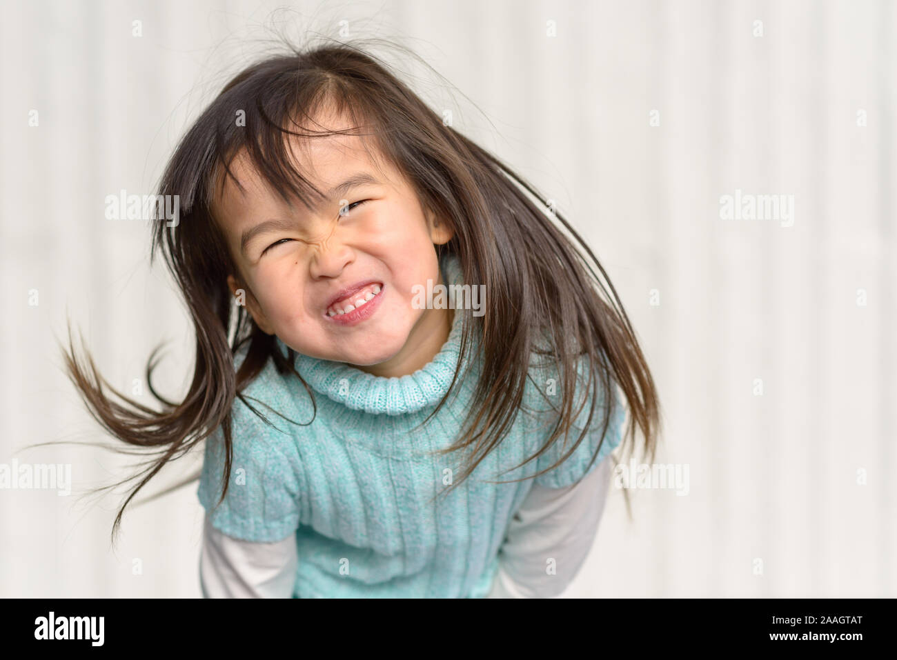 Fun loving little girl tossing her long hair as she grins at the camera ...