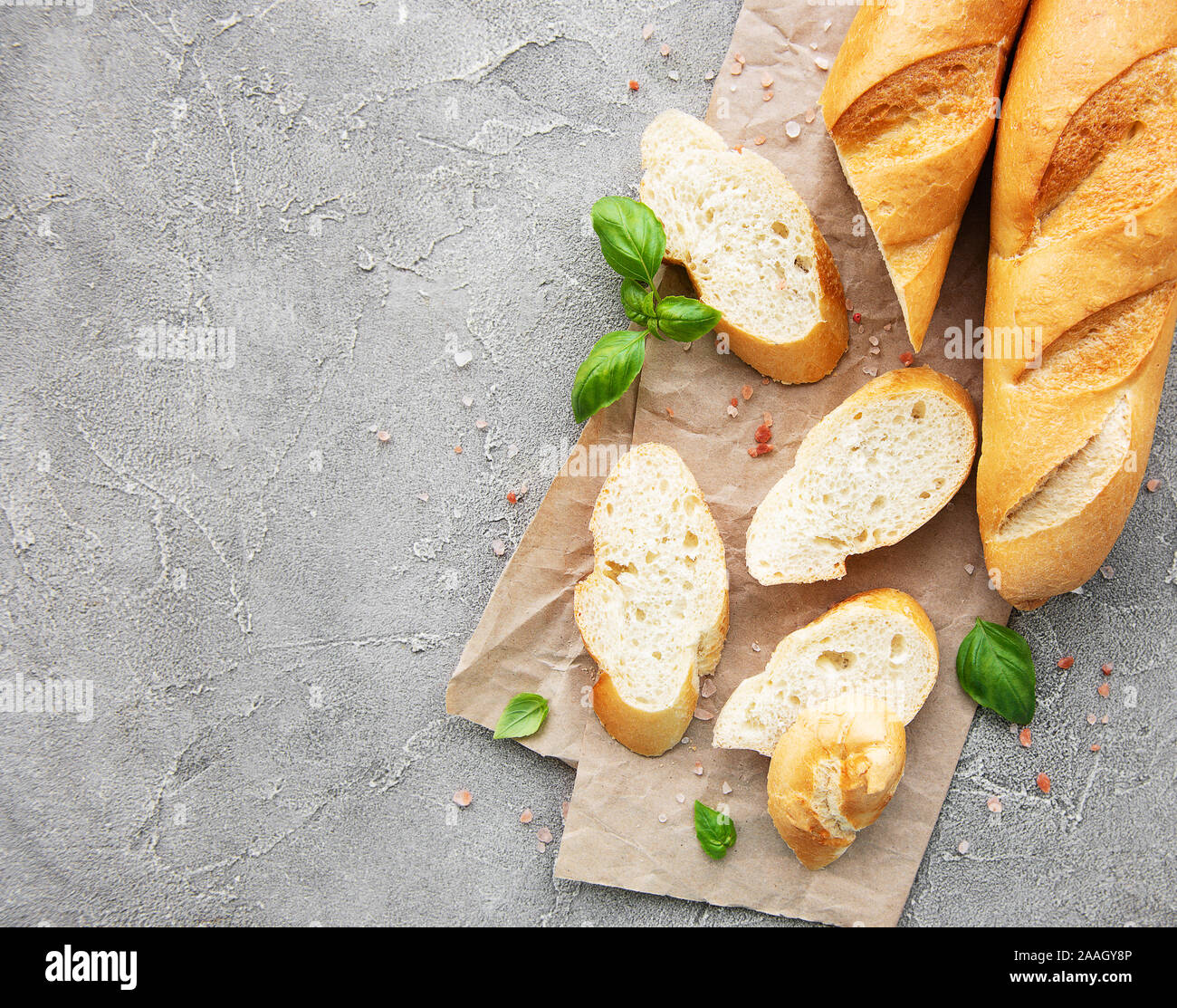 Sliced fresh crusty baguette with salt and basil on a grey concrete ...