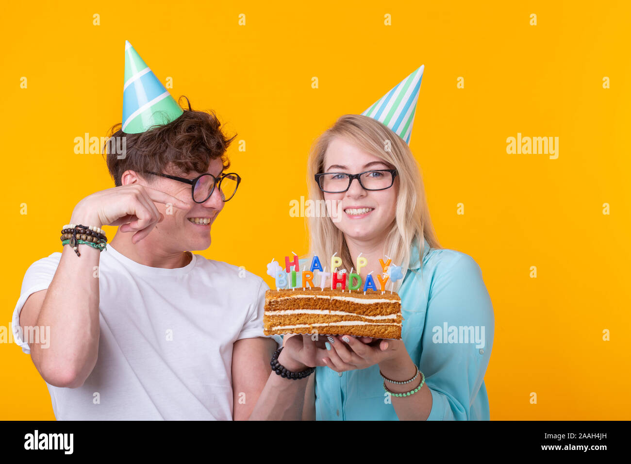 Funny young couple in paper caps and with a cake make a foolish face ...