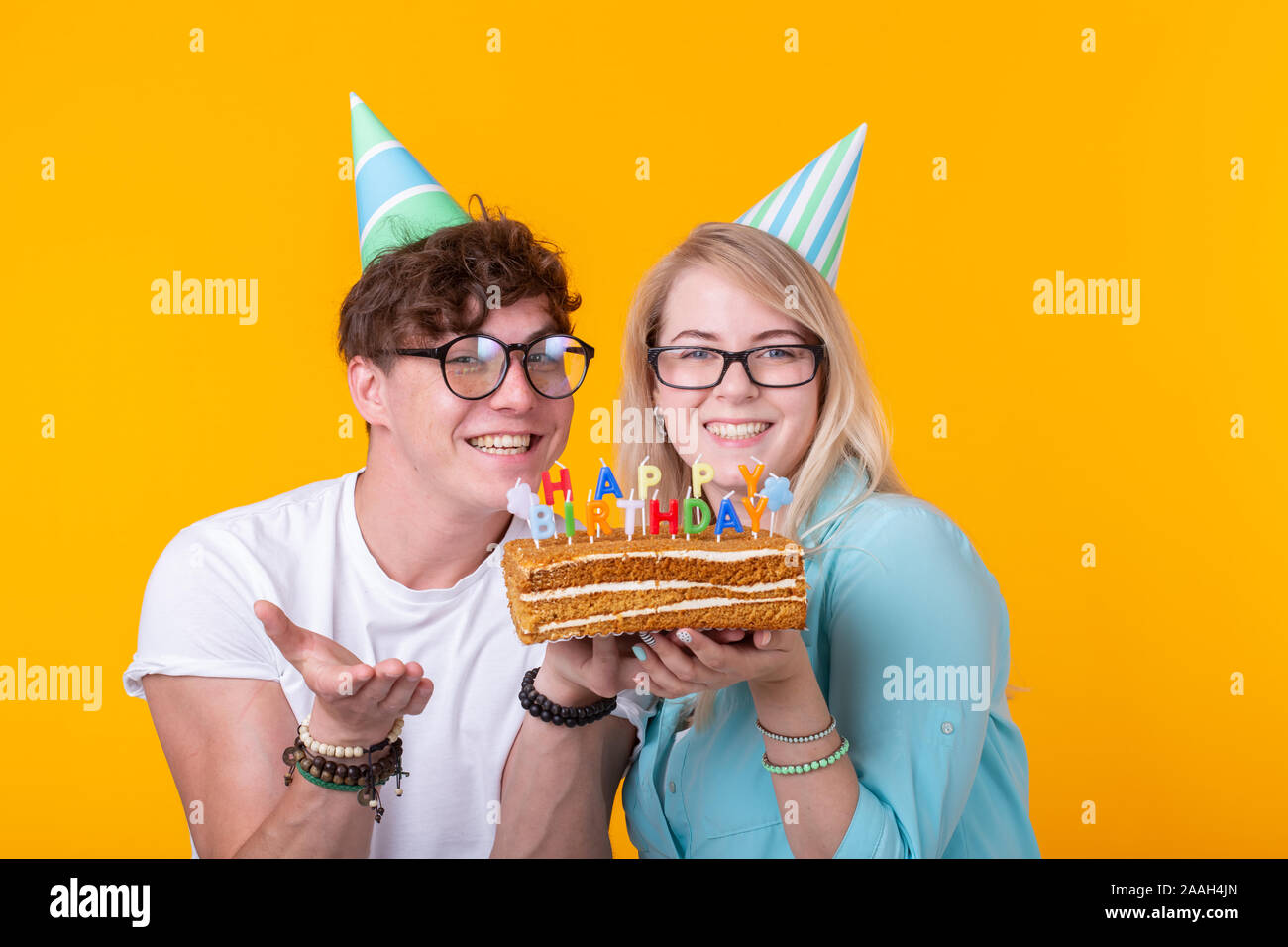 Funny young couple in paper caps and with a cake make a foolish face ...