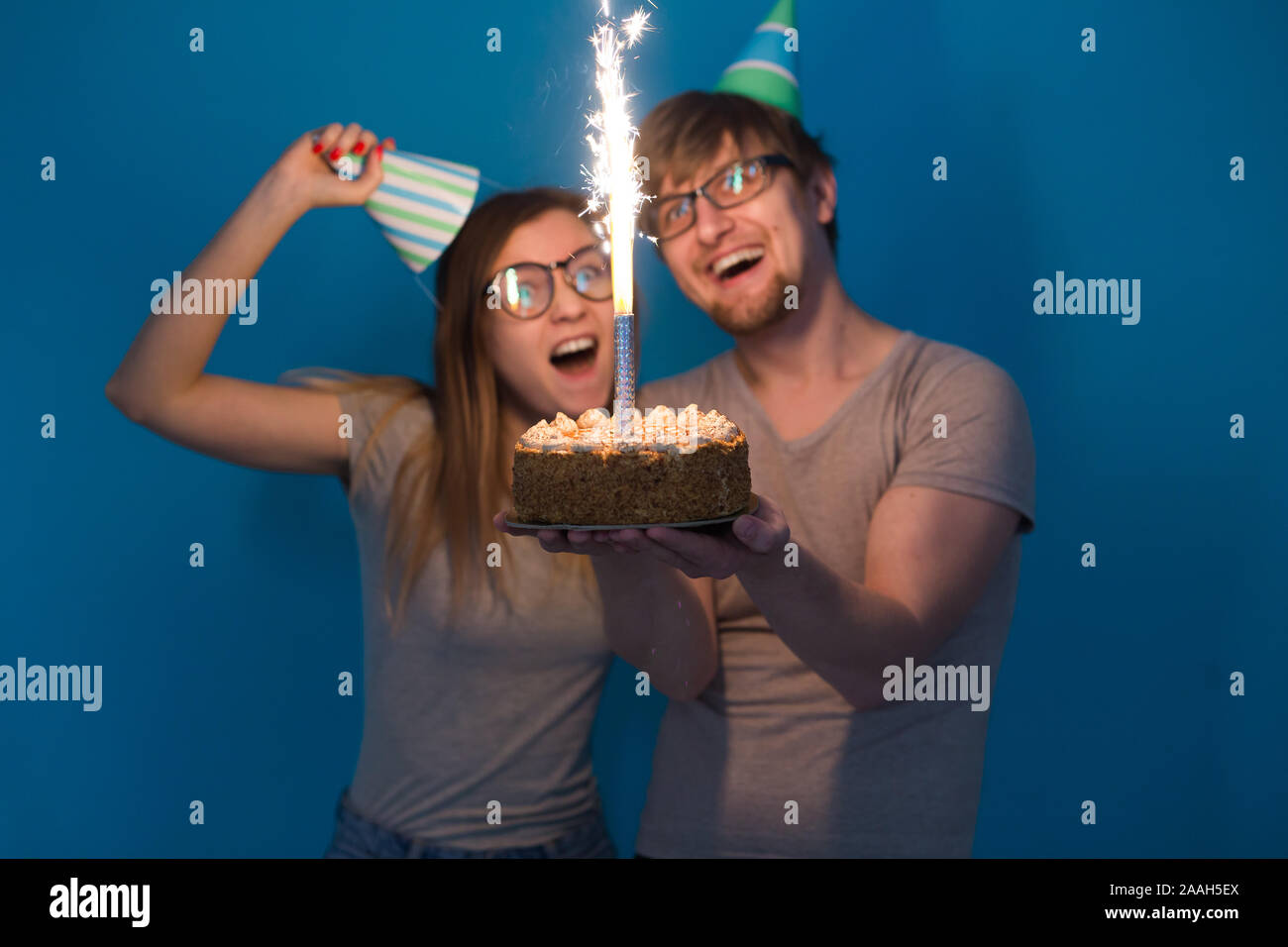 Funny young couple in paper caps and with a cake make a foolish face ...