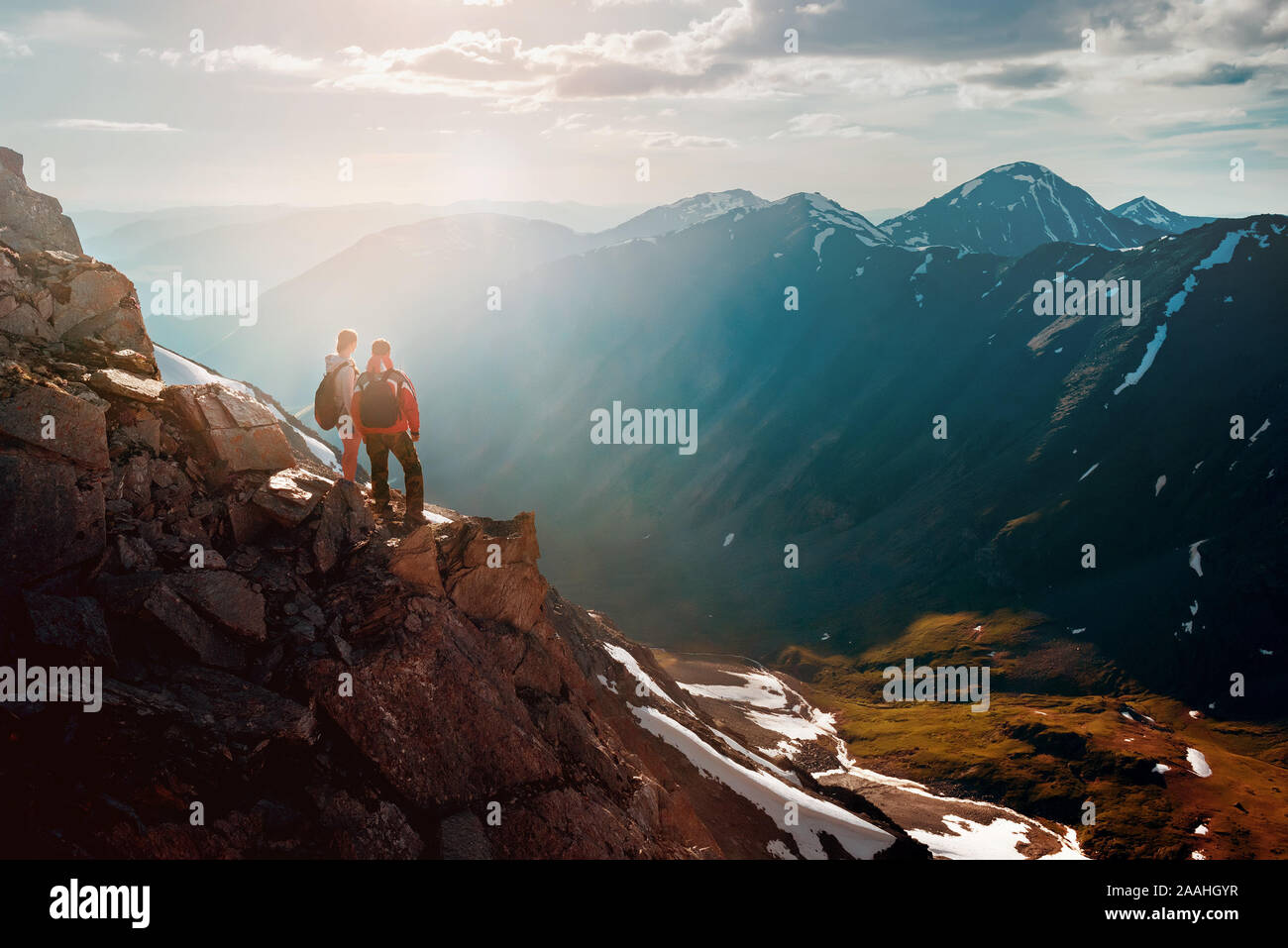 Two hikers male and female stands on a cliff in big mountains and ...