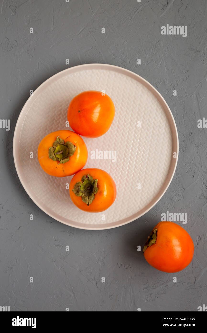 Raw Ripe Orange Persimmons on a plate over gray surface, top view. Flat ...