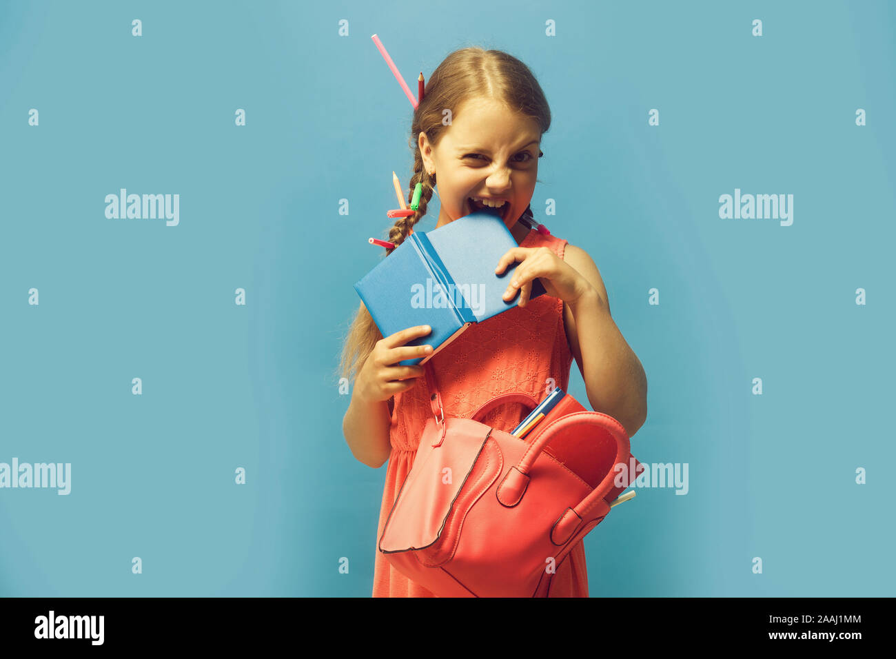 Girl with pink bag bites blue notebook. Kid with naughty face ...