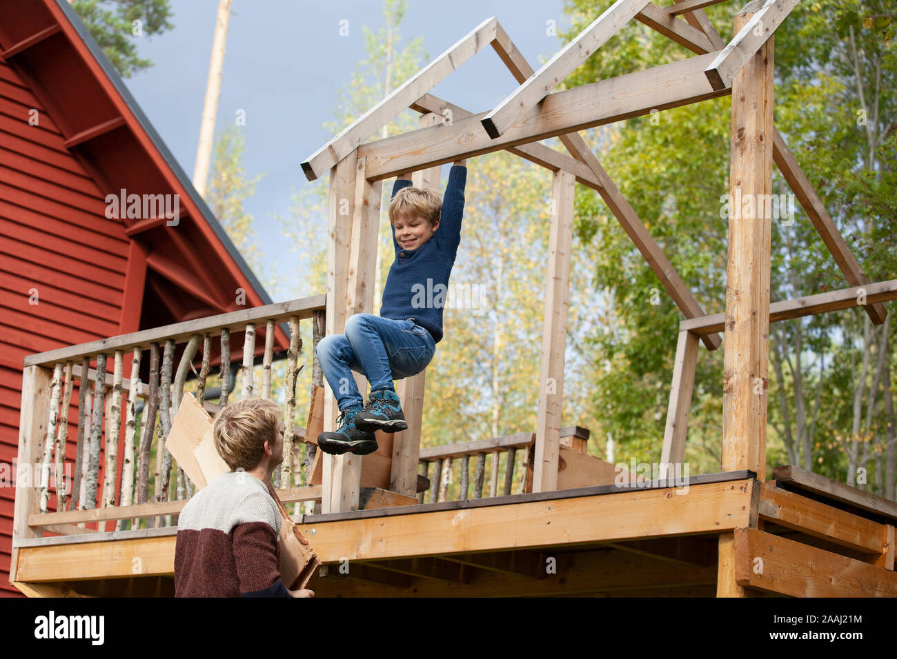 Father watching boy swinging on beam of unfinished treehouse Stock ...