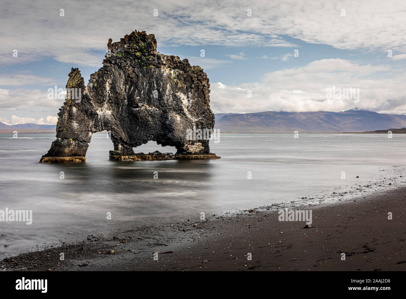 Volcanic rock formation in the shallows on a black sand beach ...