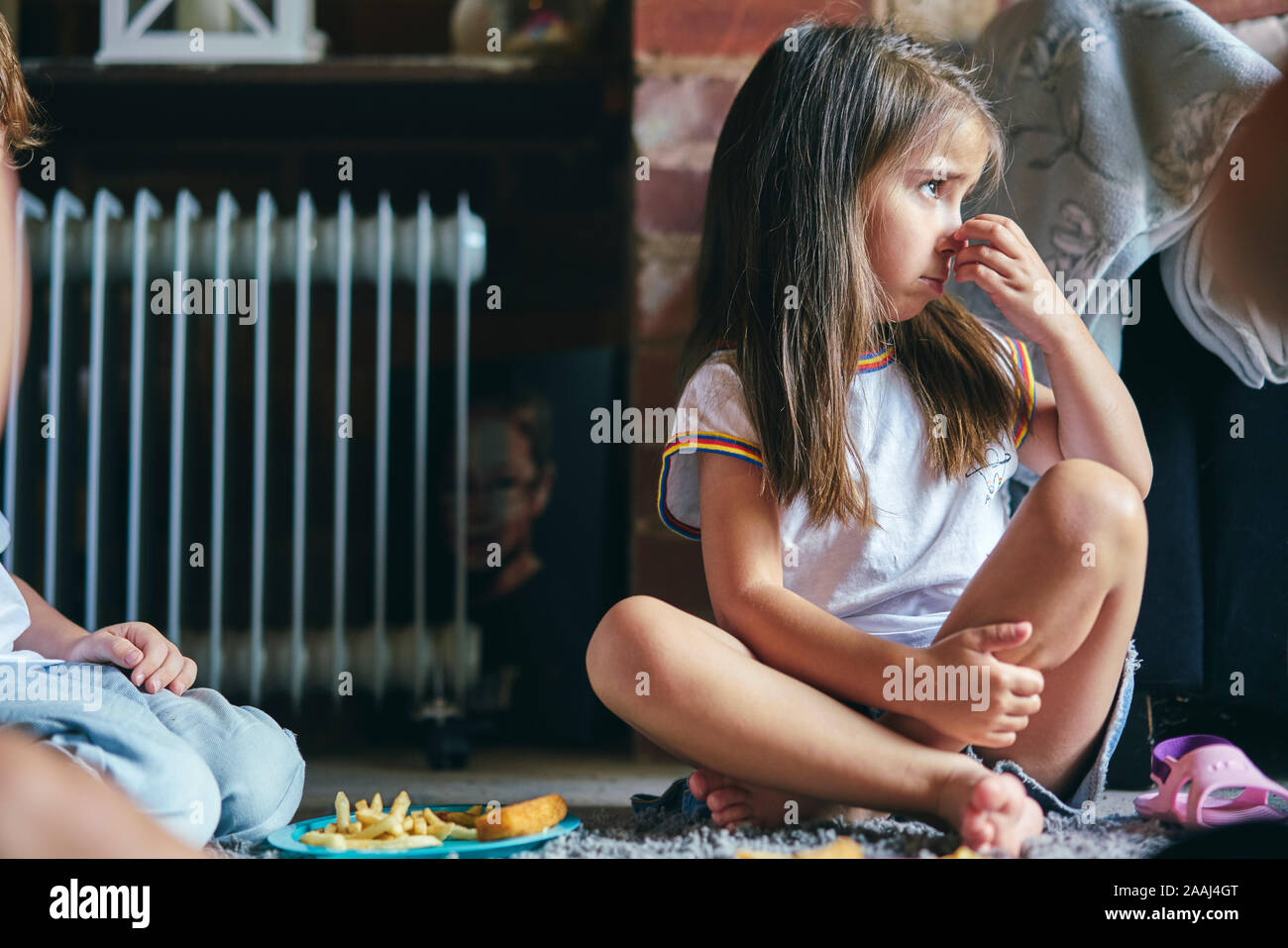 Girl sitting on rug beside radiator scratching nose Stock Photo - Alamy