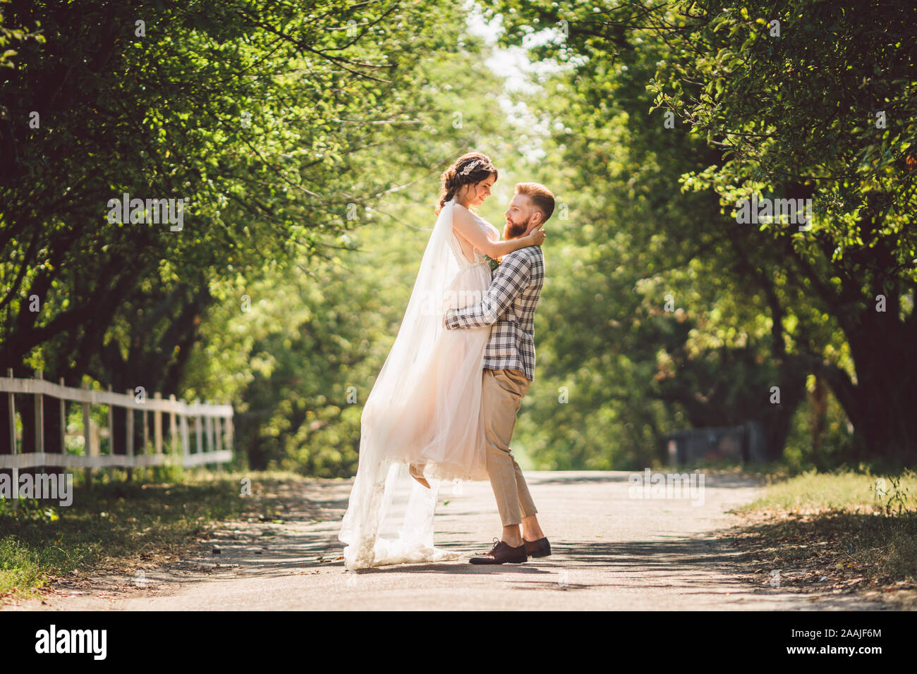 Happy bridegroom raises bride in summer park. man raised and hug woman ...