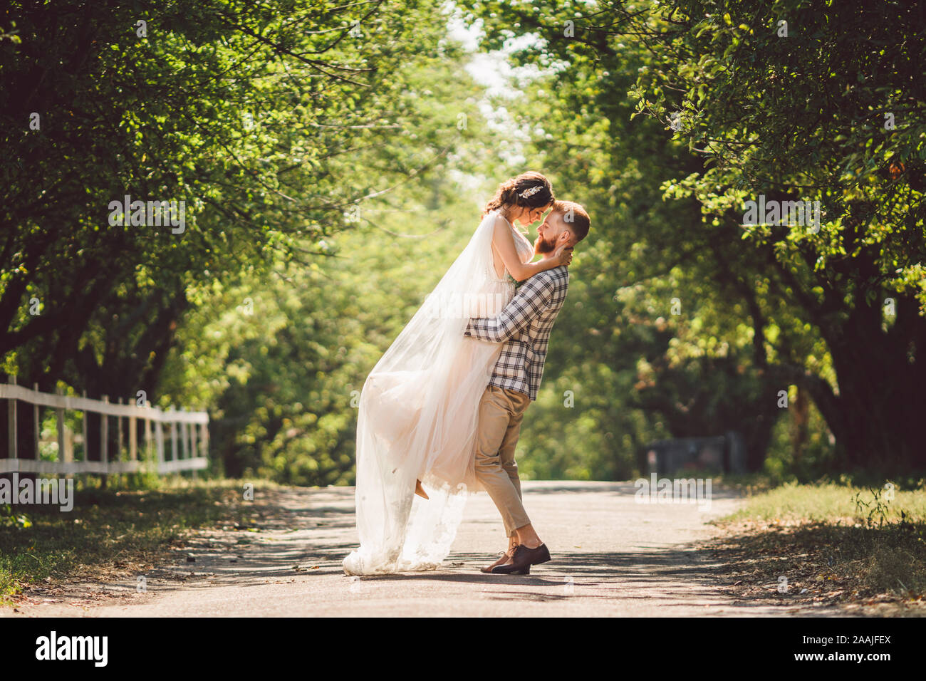 Happy bridegroom raises bride in summer park. man raised and hug woman ...