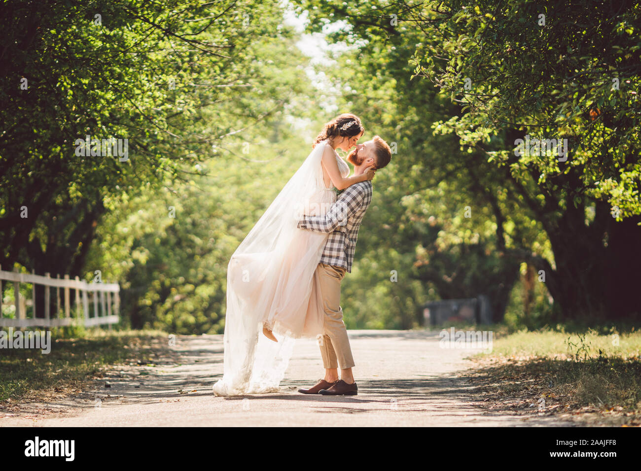 Happy bridegroom raises bride in summer park. man raised and hug woman ...