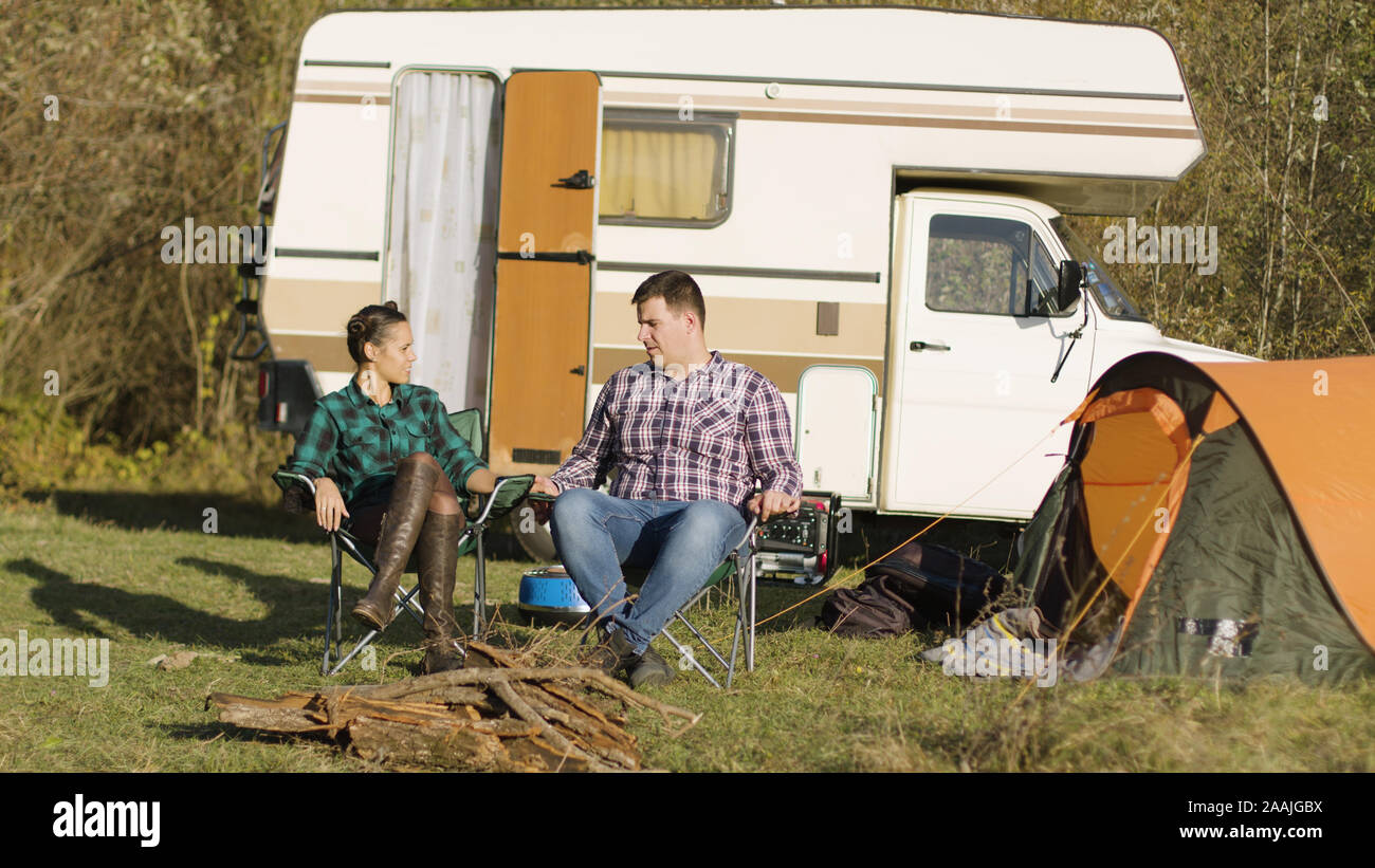 Hipster couple sitting on their camping seats and holding hands in ...