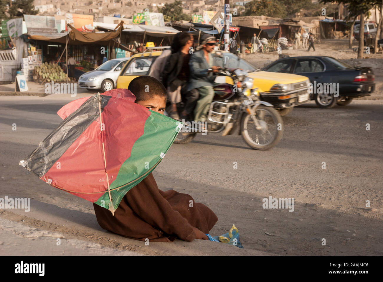 A young boy with a home made kite on his back sits on the side of a ...