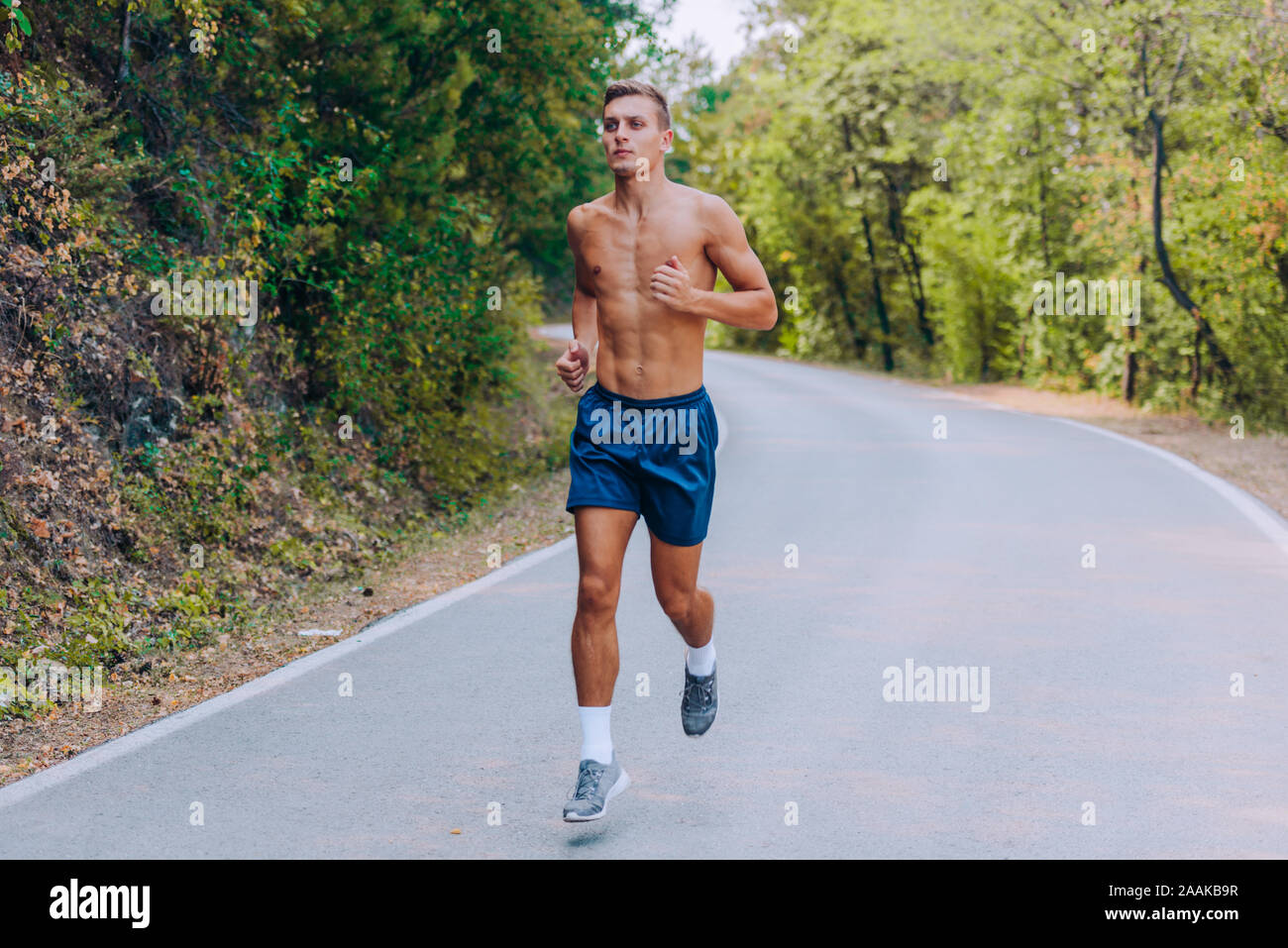 Close up of feet of young runner man running along road in the forest ...
