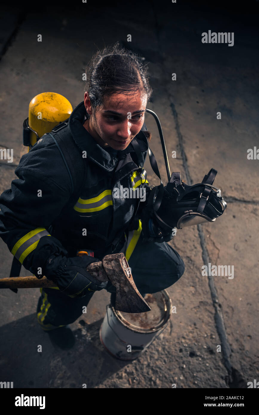 Portrait of a female firefighter while holding an axe and wearing an ...